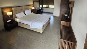 Quarto de hotel moderno com uma cama grande, ventoinha no teto, ar condicionado, televisão e um pequeno espaço de trabalho.