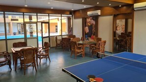 Quarto com mesa de pingue-pongue, cadeiras de vime e vista para a piscina.