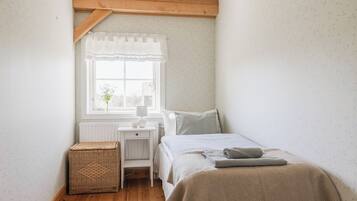 Um quarto com cama, mesa de cabeceira, luminária, janela com vista e cesto de vime.