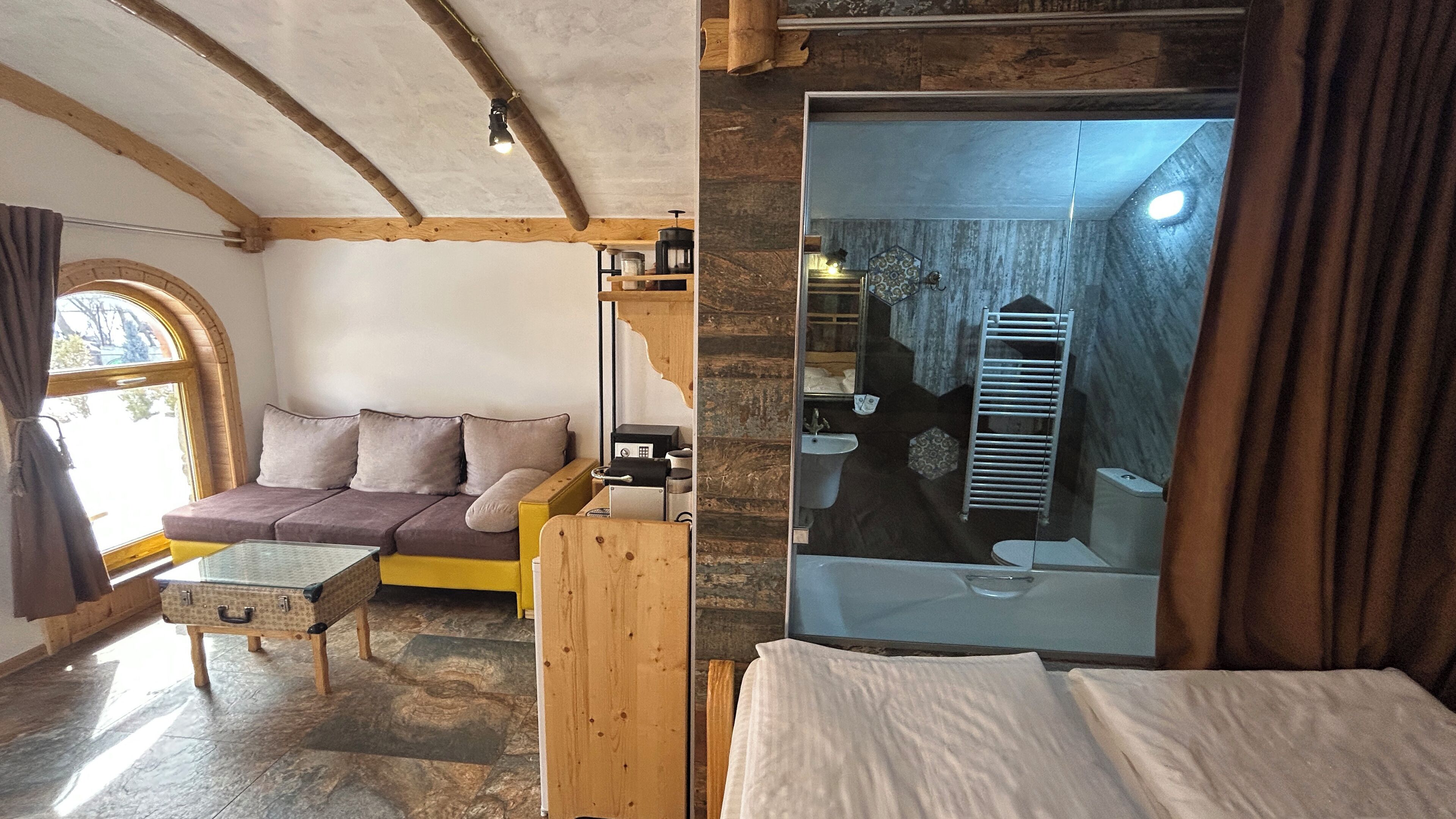 Um quarto aconchegante com teto de madeira, um sofá, uma mesa pequena e uma cama.