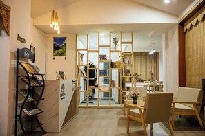 Quarto de hotel com balcão de madeira, estante de livros, área de refeições com mesa e cadeiras, e vista através de um separador.