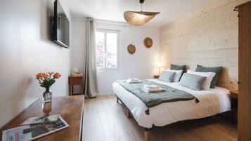 Quarto com cama, mesas de cabeceira, TV fixada na parede, janela com cortinas e uma parede de madeira.
