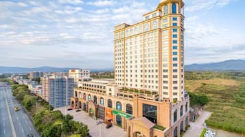 Um hotel com vários andares e um pátio central, rodeado por vegetação e um céu claro.