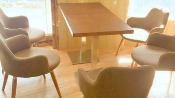 Quarto com uma mesa de madeira cercada por quatro cadeiras, um separador de vidro e vista pela janela.