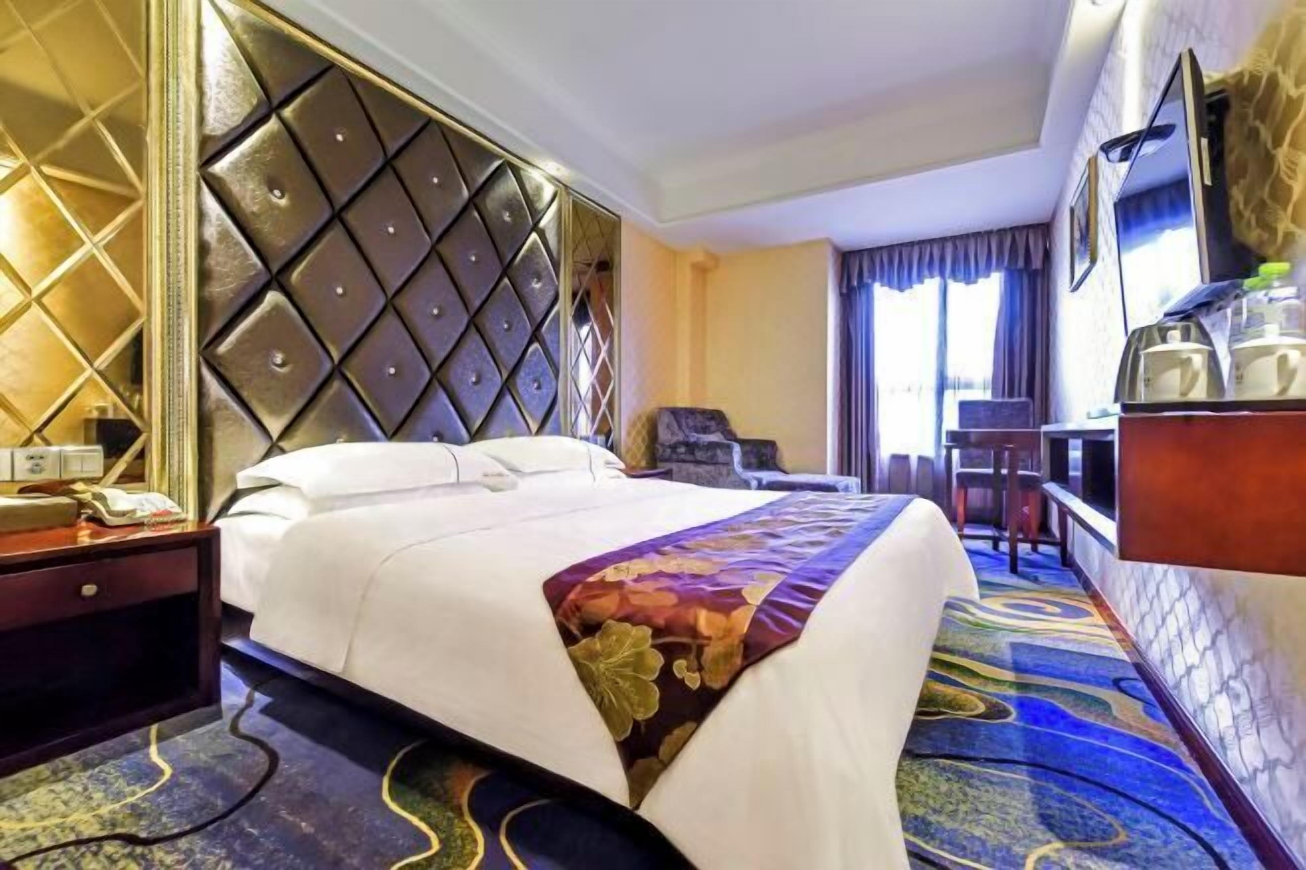 Quarto de hotel com cama grande, televisão, escrivaninha com telefone e janela com cortinas.