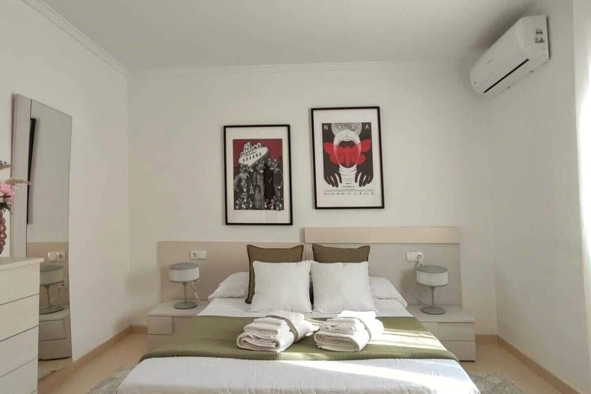 Quarto moderno com cama, mesas de cabeceira e duas imagens emolduradas na parede.