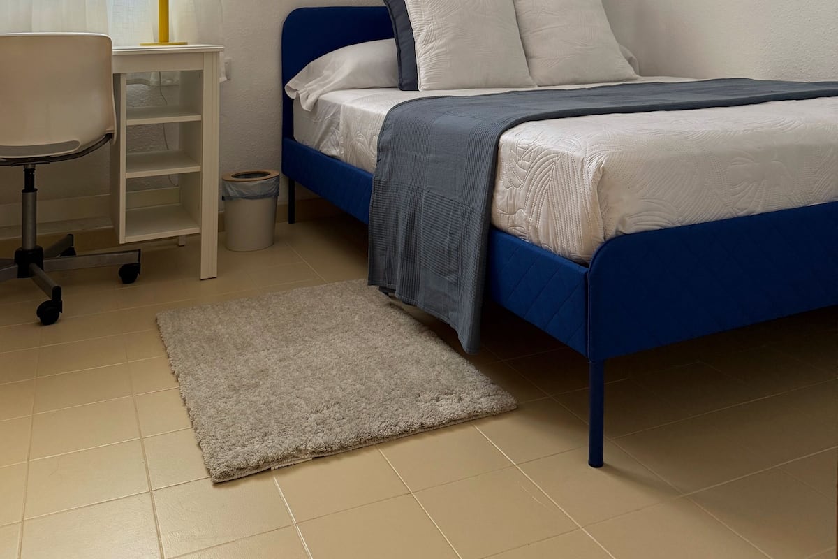 Quarto com uma cama, escrivaninha, cadeira, armário pequeno e lixeira.