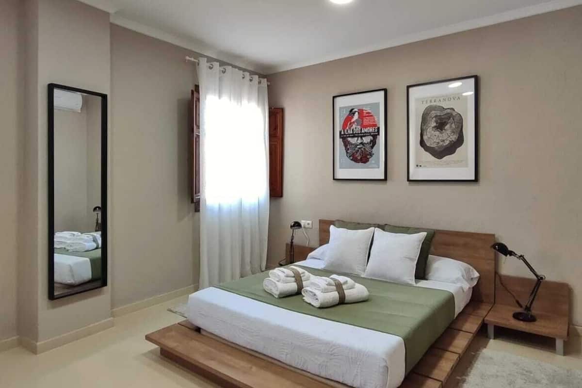 Quarto moderno com cama, mesa de cabeceira, espelho e duas molduras na parede.