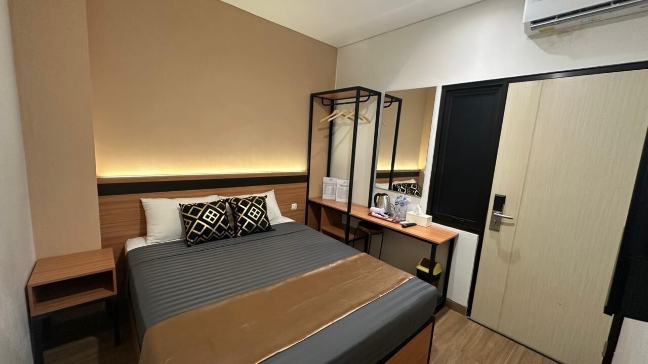 Quarto de hotel com cama, mesa de cabeceira, escrivaninha, armário e espelho.