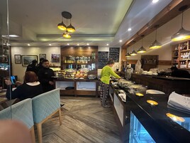 Interior de restaurante com balcão, área de estar e quadro de cardápio.