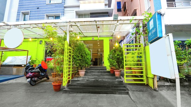 Entrada de hotel com fachada verde, plantas em vasos e uma motocicleta estacionada na frente.