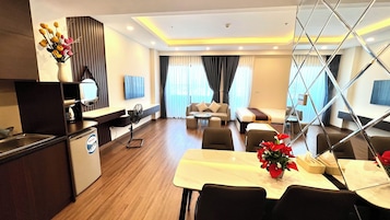 Quarto de hotel moderno com área de refeições, sofá, cama e televisão.