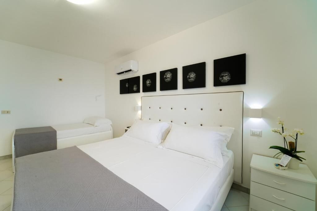 Quarto com uma cama grande, uma mesinha de cabeceira com abajur e outra mesinha de cabeceira com uma planta.