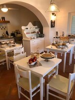 Uma sala de jantar com mesas e cadeiras brancas, um buffet montado e um arco decorativo.
