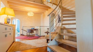 Interior moderno com escada de madeira, guarda-corrimão de vidro e área de jantar com tapete vermelho.