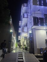 Um edifício com várias varandas decoradas com luzes de cordão, uma placa com informações de contato e uma escadaria que leva à entrada.