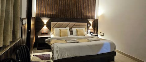 Quarto de hotel moderno com uma cama grande, um ventilador de teto, uma mesinha e um espaço de estar com uma poltrona.