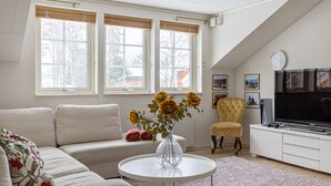 Uma sala de estar com sofá, mesa de centro com um vaso de flores, televisão e uma cadeira.