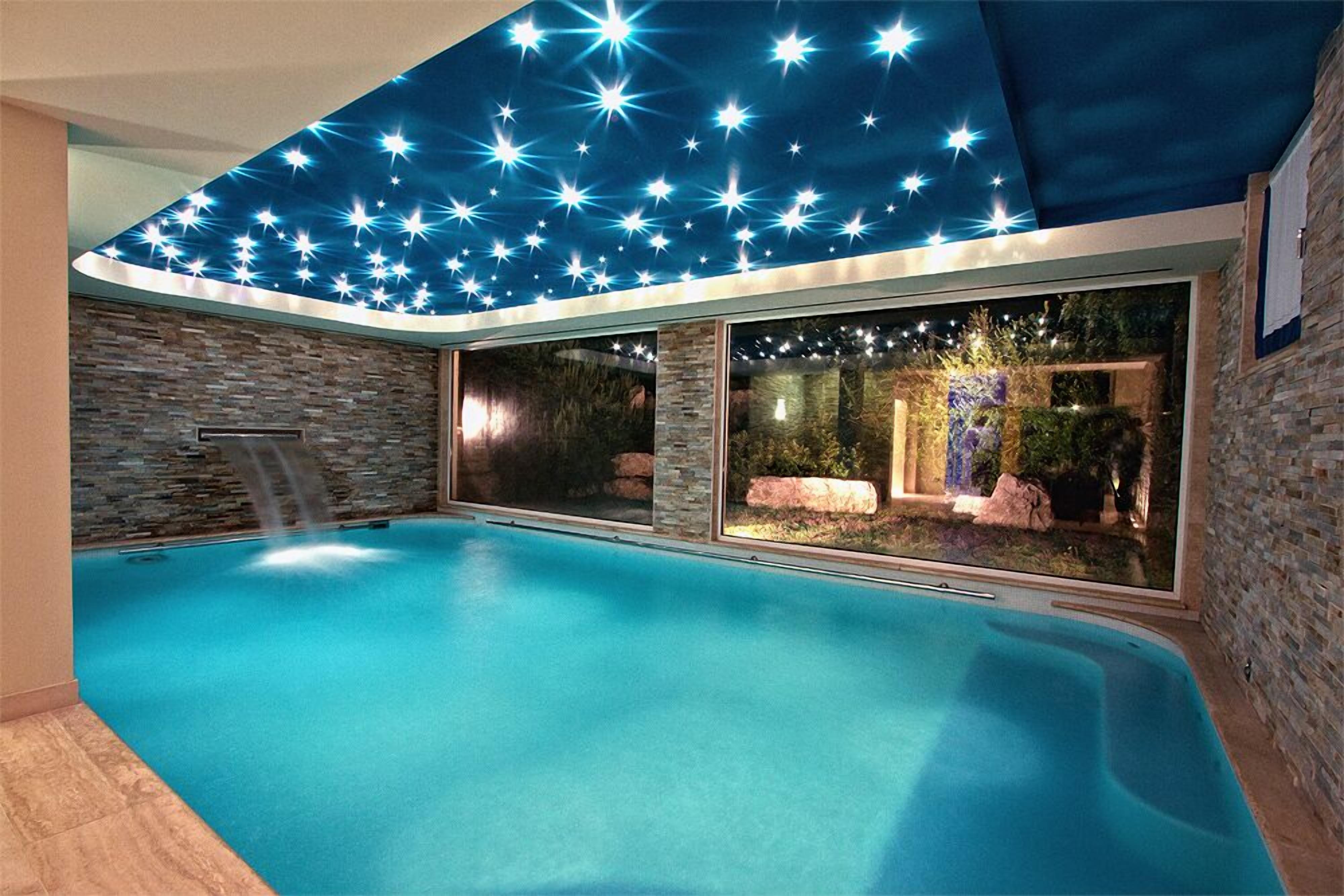 Piscina interior com teto estrelado e vista para um jardim paisagístico.