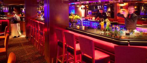 Uma área de bar com iluminação vermelha, banquetas e um bartender.