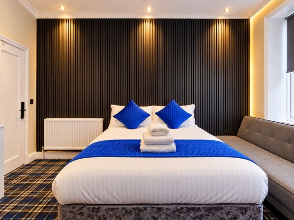 Quarto de hotel com uma cama grande, um radiador, um sofá e uma janela.
