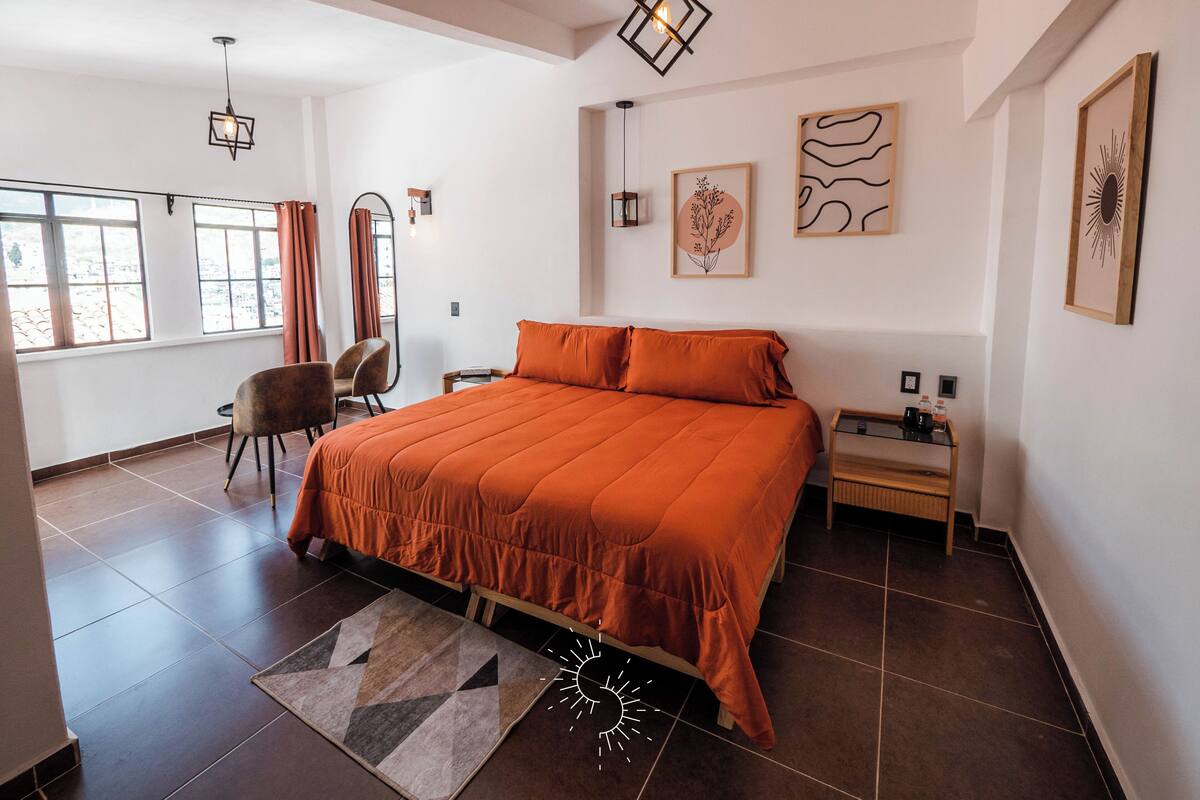Um quarto moderno com uma cama grande, uma poltrona, uma mesinha de cabeceira e um espelho fixado na parede.