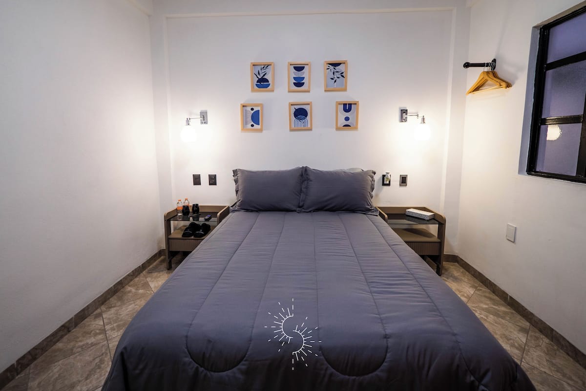 Quarto de hotel bem arrumado com uma cama grande, mesa de cabeceira com abajur e luminária na parede.