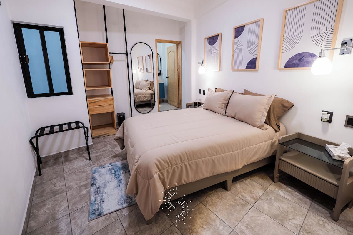 Quarto com cama, mesa de cabeceira, espelho, guarda-roupa e um pequeno espaço de estar.