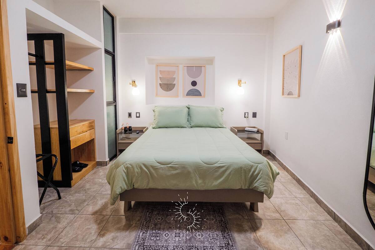 Quarto com cama, mesas de cabeceira, luminária na parede e porta para um armário.