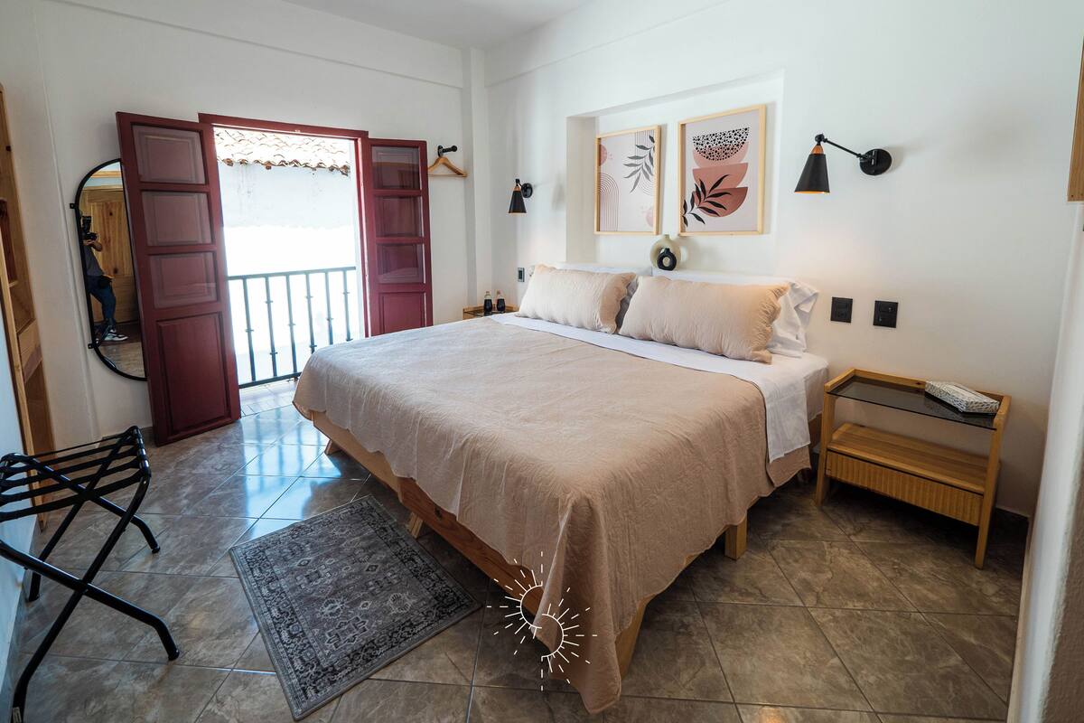 Um quarto com uma cama, mesa de cabeceira, espelho, porta e janela.