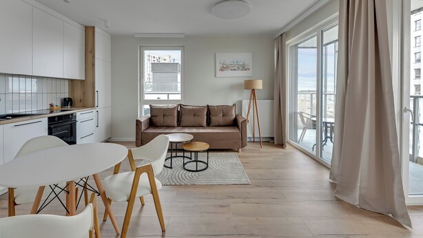 Um apartamento moderno com cozinha, sala de jantar e sala de estar. Possui janelas amplas, um sofá e um abajur.