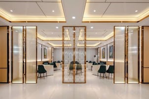 Sala de conferências de hotel com uma mesa central rodeada por cadeiras, dividida por painéis de vidro e equipada com iluminação no teto.