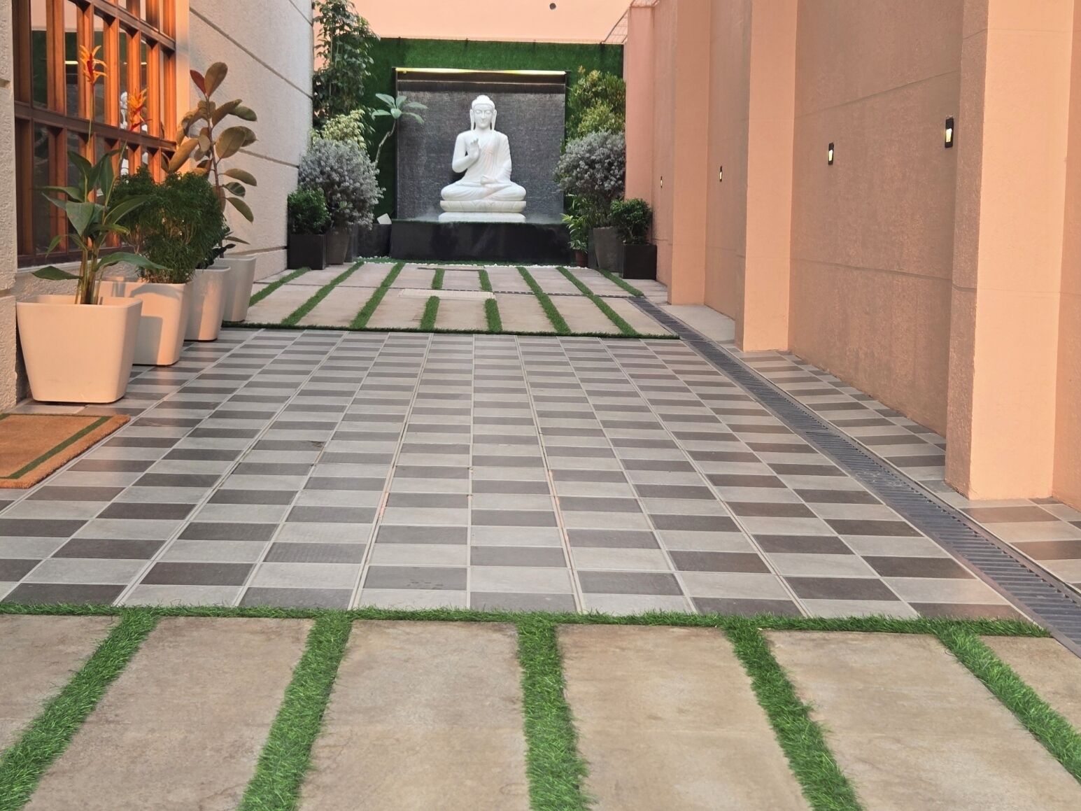 Um pátio com estátua de Buda, plantas em vasos e um caminho de ladrilhos.