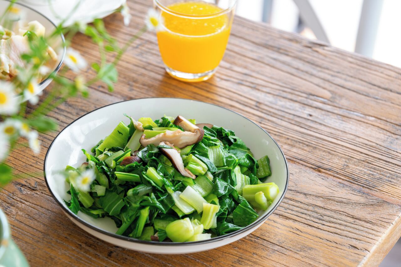 Prato de vegetais verdes folhosos com cogumelos sobre uma mesa de madeira.
