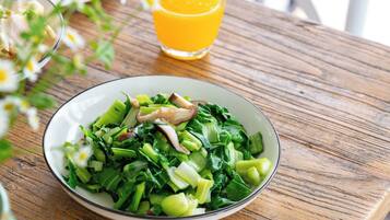 Prato de vegetais verdes folhosos com cogumelos sobre uma mesa de madeira.