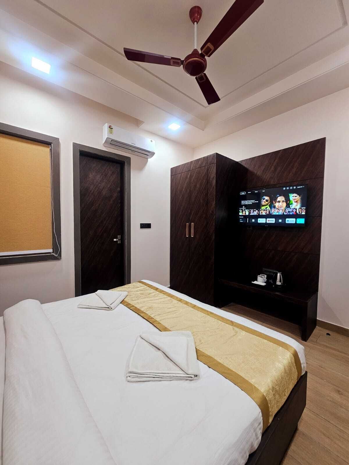 Quarto de hotel com cama, televisão, ventoinha no teto e ar condicionado.