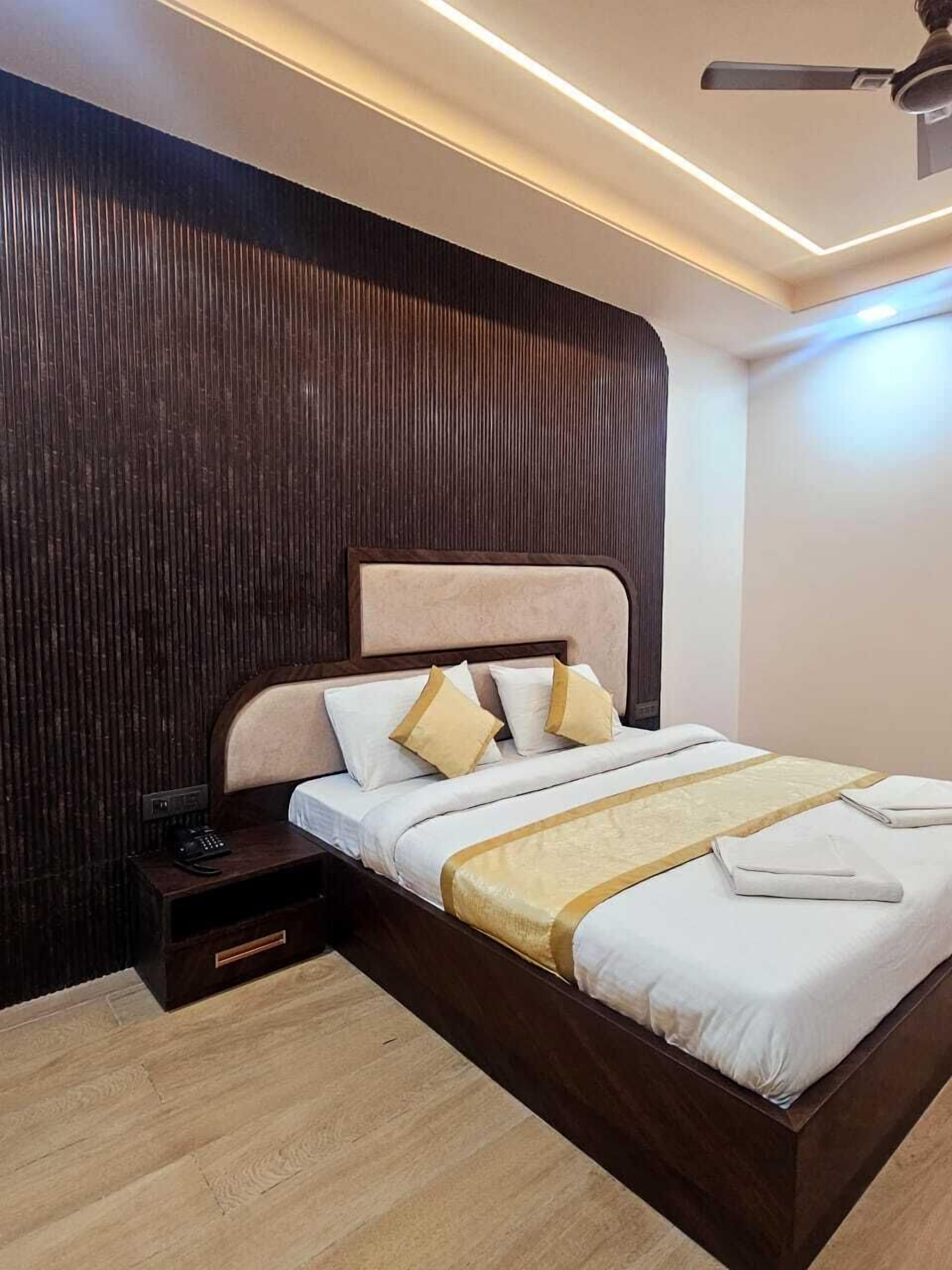 Quarto com cabeceira de madeira, mesa de cabeceira com telefone e cama com roupa de cama branca e detalhes dourados.