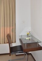 Um quarto pequeno e moderno, com uma mesa de vidro, uma cadeira de madeira e um vaso com flores.