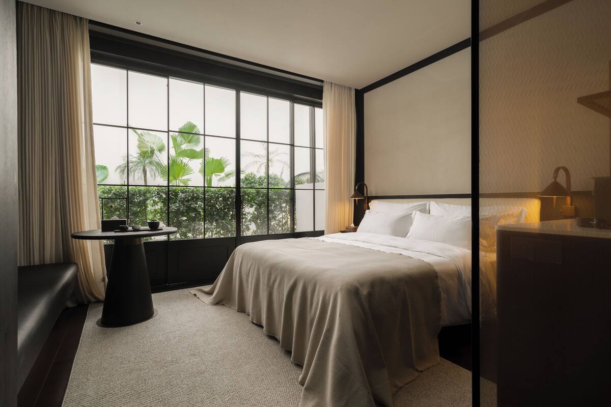 Quarto de hotel moderno com uma grande janela, uma cama, mesa de cabeceira e escrivaninha.