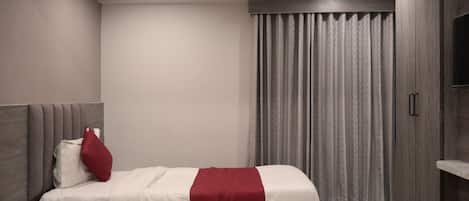 Quarto de hotel com cama, ventoinha no teto e janela com cortinas.