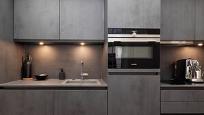 Uma cozinha moderna com armários cinza, forno embutido e máquina de café.