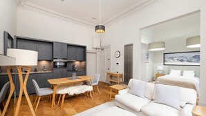 Quarto de hotel moderno com área de refeições, sofá, cama e uma janela grande com vista para as montanhas.