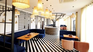 Interior moderno de restaurante com piso riscado, assentos em azul e rosa, e várias luminárias pendentes.