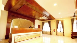 Uma área de recepção de hotel com um balcão de madeira, um biombo decorativo estampado e um chão limpo e lustroso.