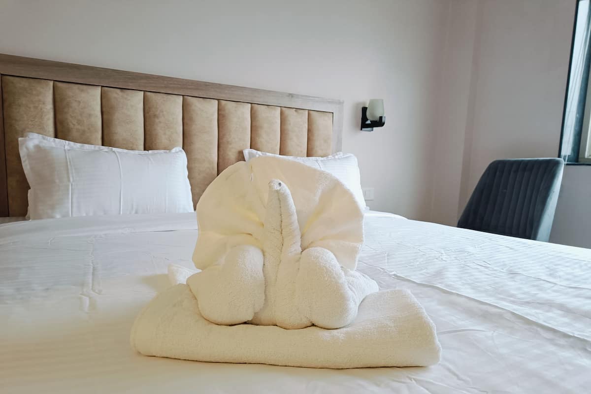 Cama bem arrumada com uma decoração de toalhas no centro, cabeceira acolchoada e luminária fixada na parede.