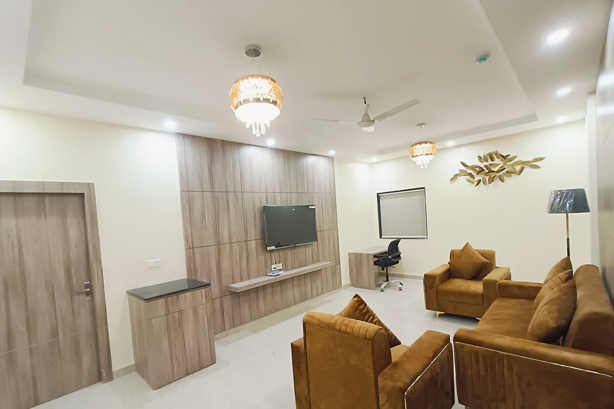Uma sala de estar moderna com televisão de tela plana, painéis de parede de madeira, ventilador de teto e sofás estofados marrons.