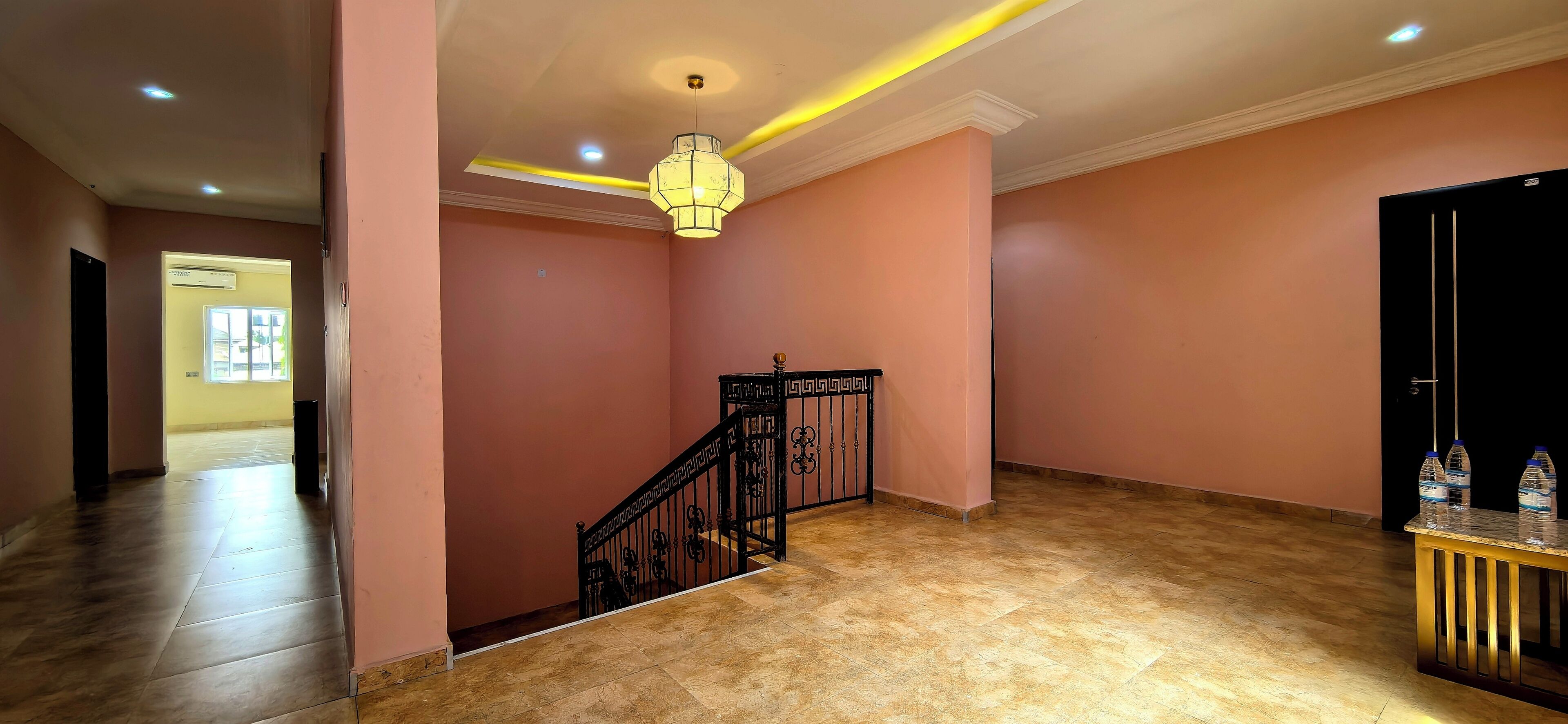 Um corredor com paredes cor-de-rosa, escada com corrimãos pretos e teto com iluminação embutida.