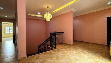 Um corredor com paredes cor-de-rosa, escada com corrimãos pretos e teto com iluminação embutida.
