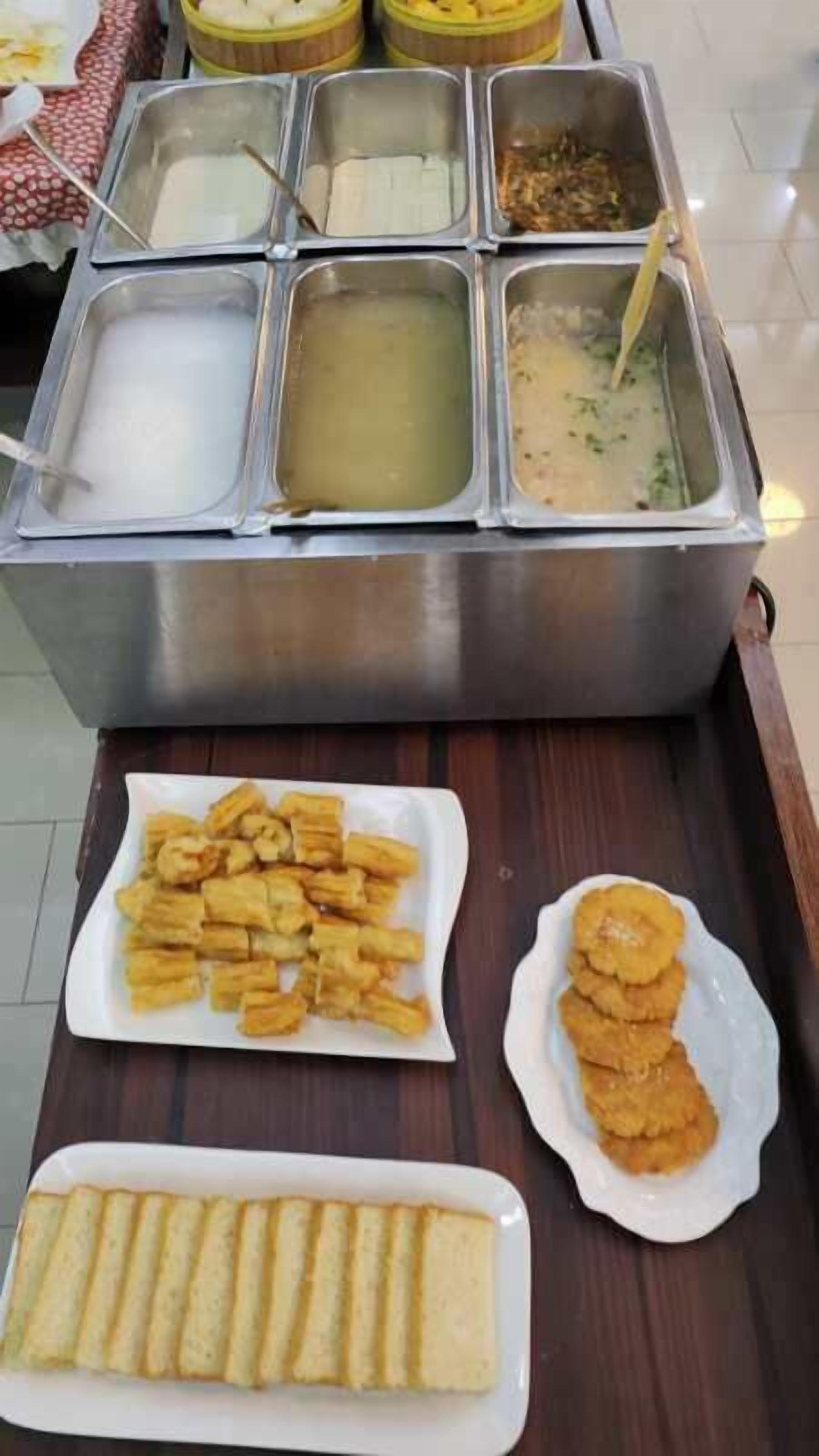 Buffet com diversos pratos, incluindo frituras, um prato branco com um prato em camadas e uma bandeja com frituras.