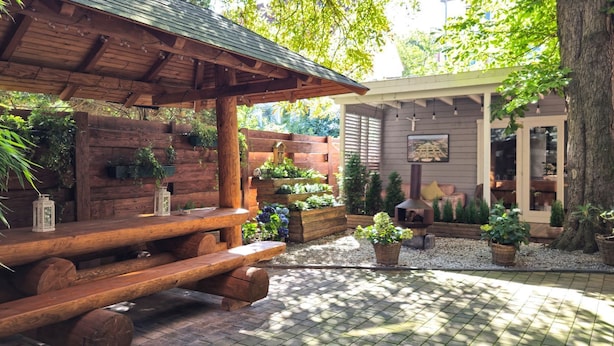 Uma pérgola de madeira com bancos, rodeada por vasos de plantas e uma lareira.